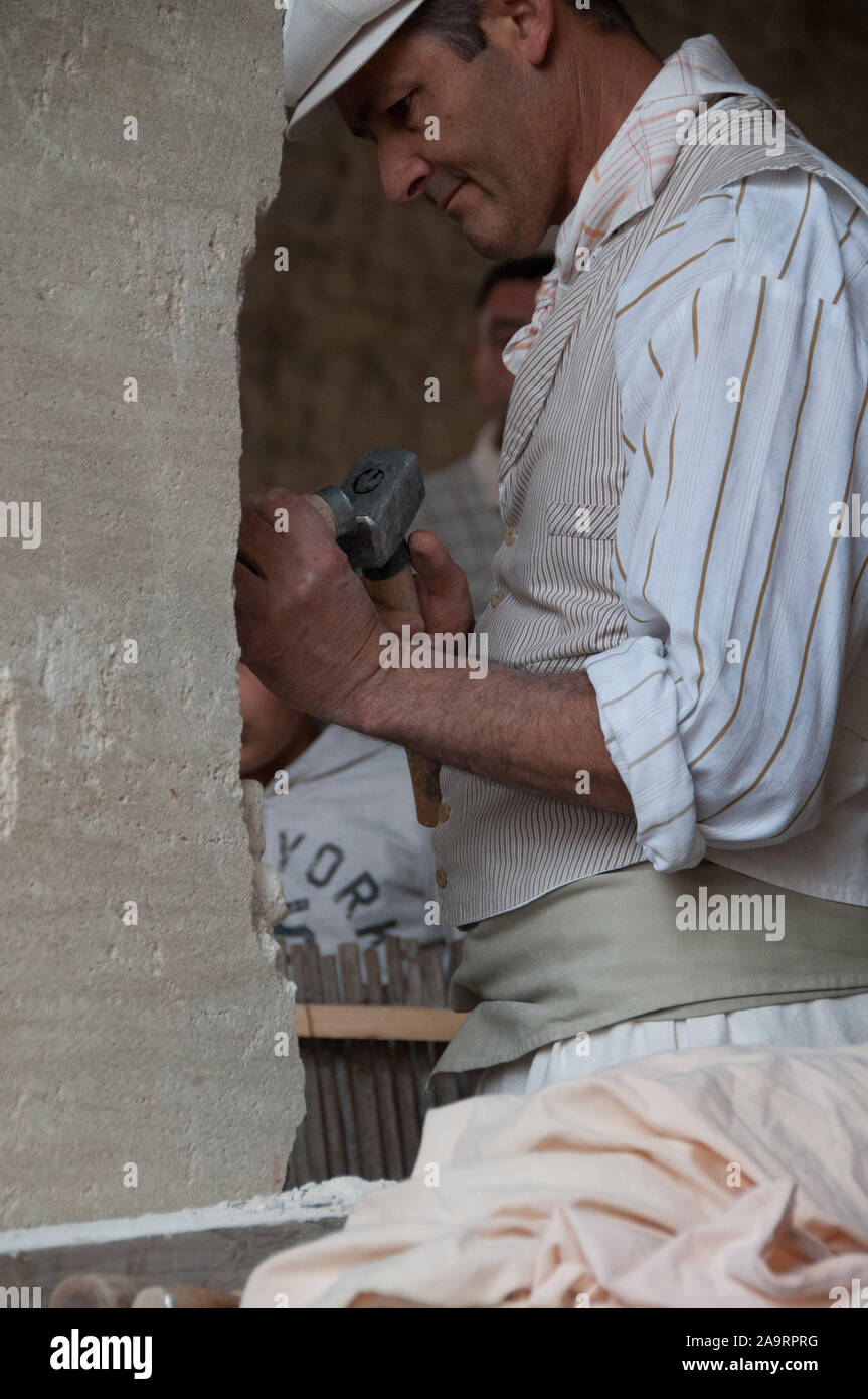 stone mason dressed up in old fashioneed clothes,carving a stone block ...