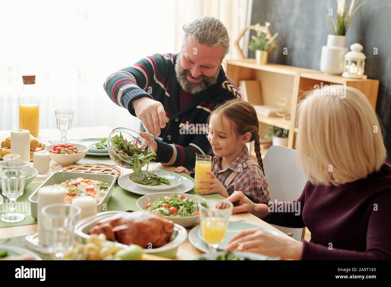 Happy grandpa giving salad to his cute granddaughter by festive table ...
