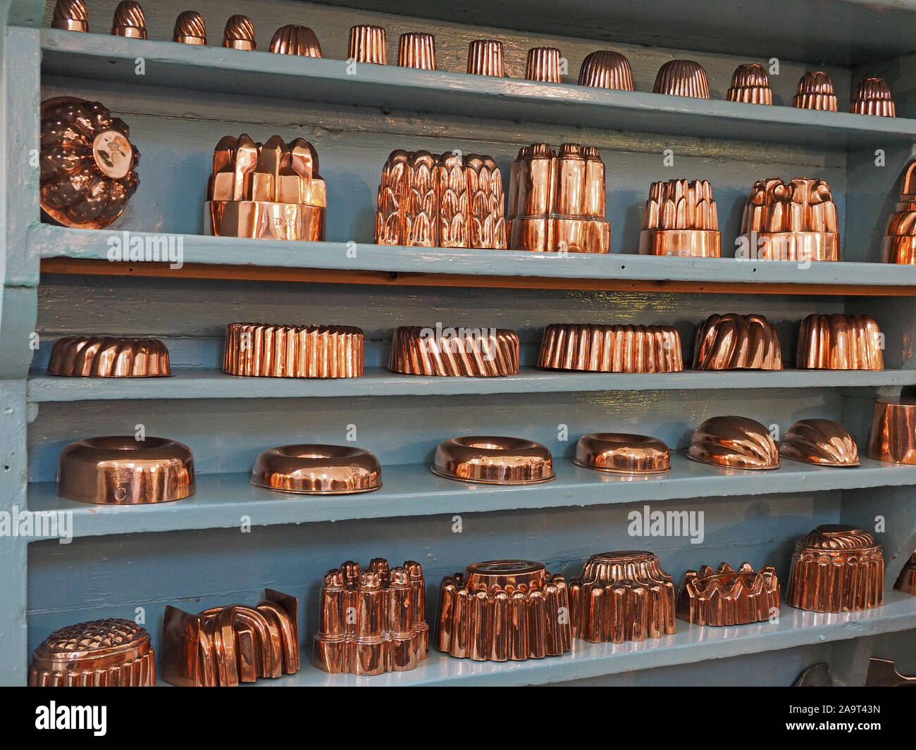 extensive display of copper pudding and jelly moulds on blue shelves in ...