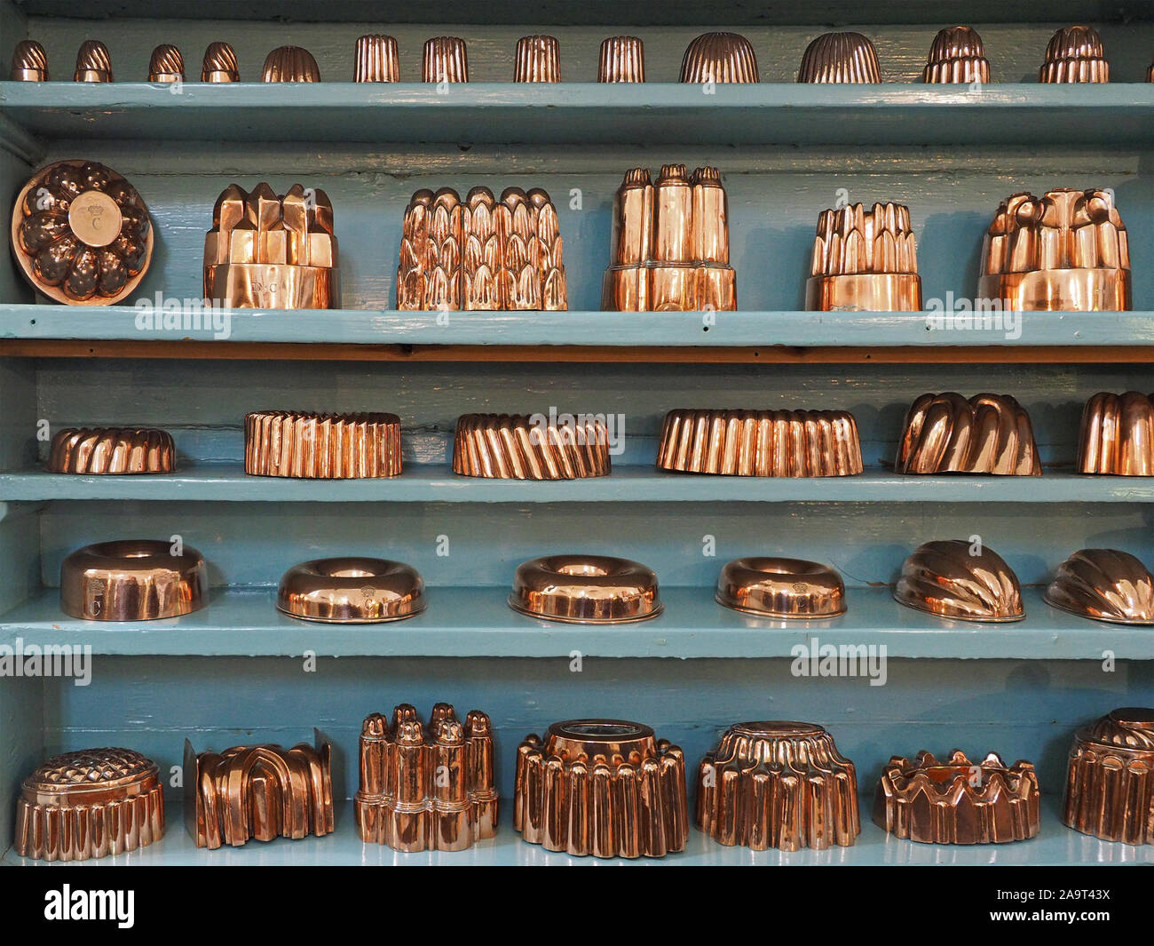 extensive display of copper pudding and jelly moulds on blue shelves in ...