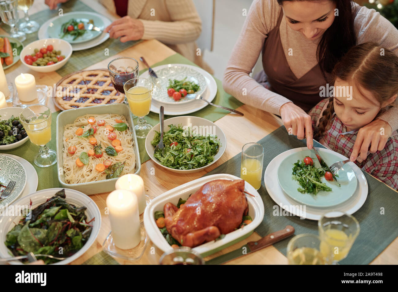 Young mother cutting tomato on plate of her little daughter by family ...