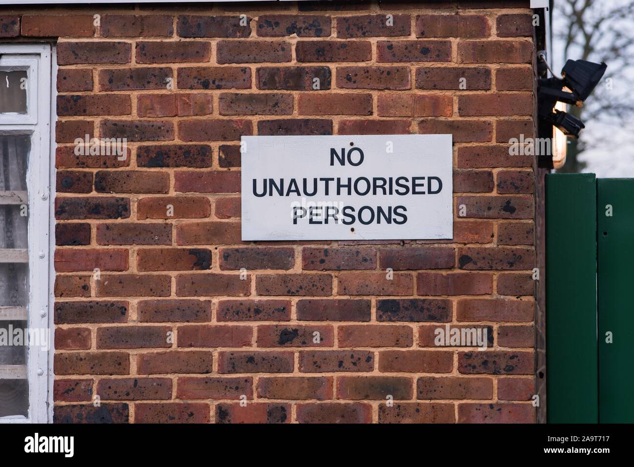 "No Unauthorised persons" sign board on a wall with black text on white ...