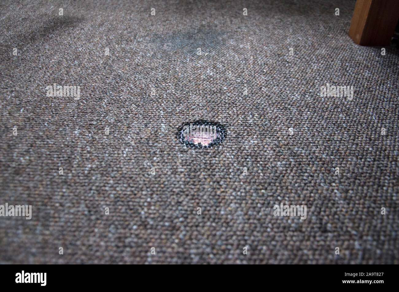 A burned hole in an old stained brown carpet Stock Photo - Alamy