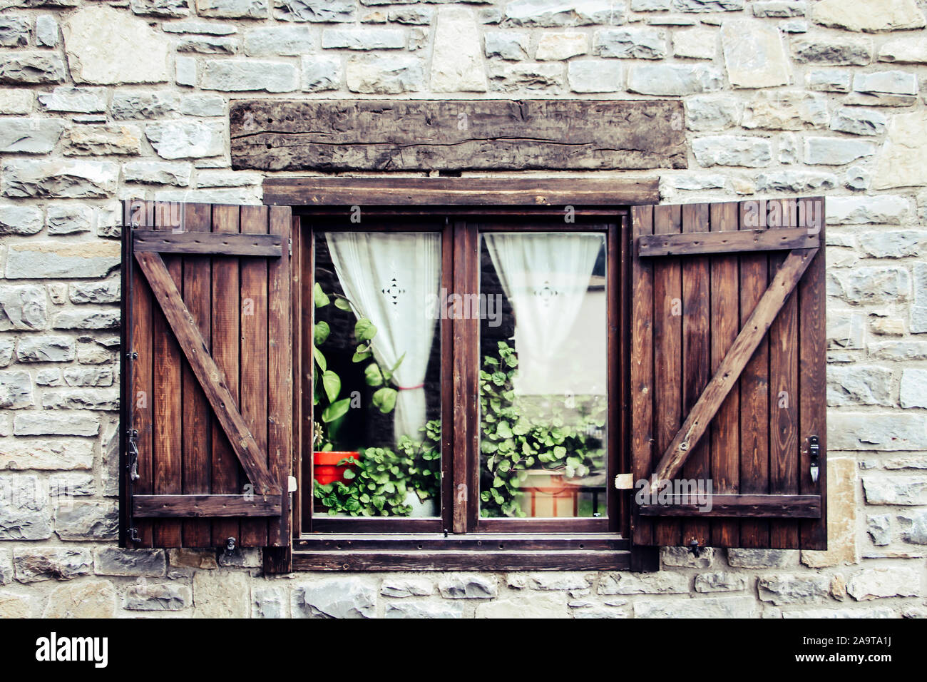 Beautiful wooden window of a stone house with plants and curtains ...