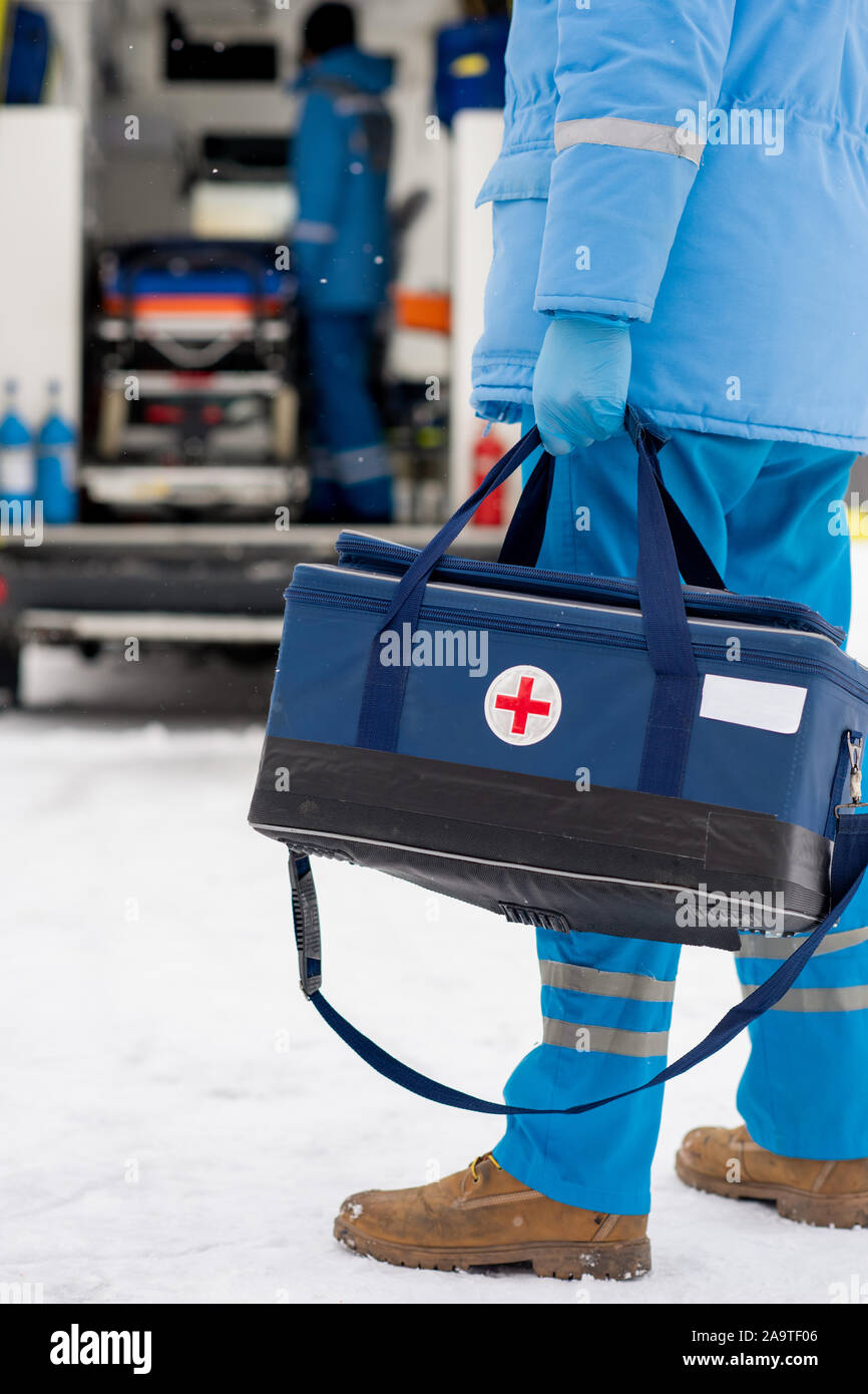Young paramedic in blue workwear and medical gloves carrying first aid ...