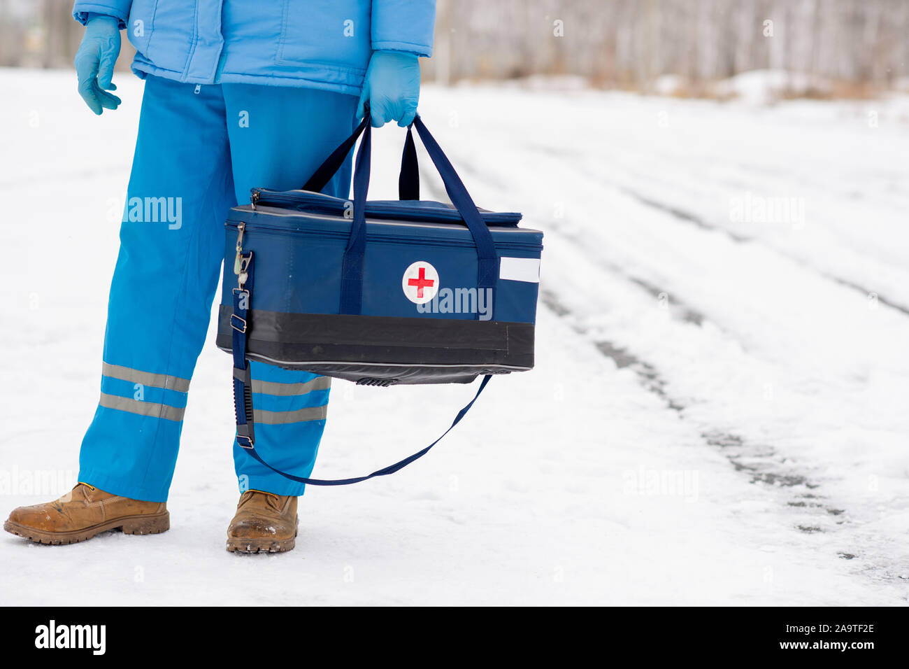 Young paramedic in blue workwear holding first aid kit with red cross ...