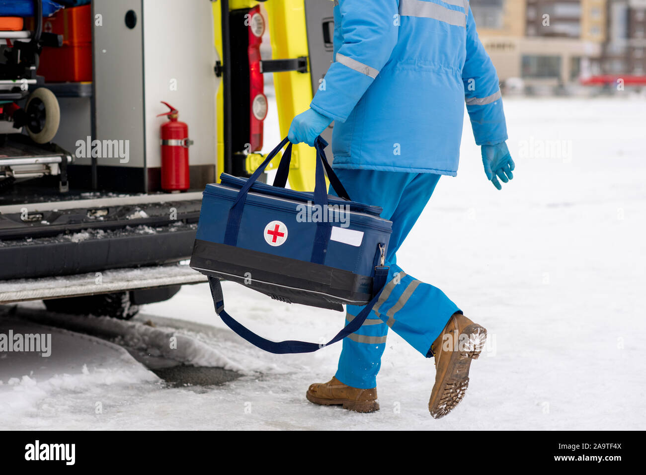 Male paramedic in blue workwear and gloves carrying first aid kit with ...