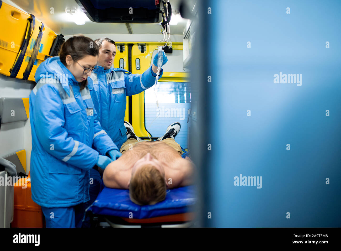 Paramedic examining unconscious shirtless man while colleague holding ...