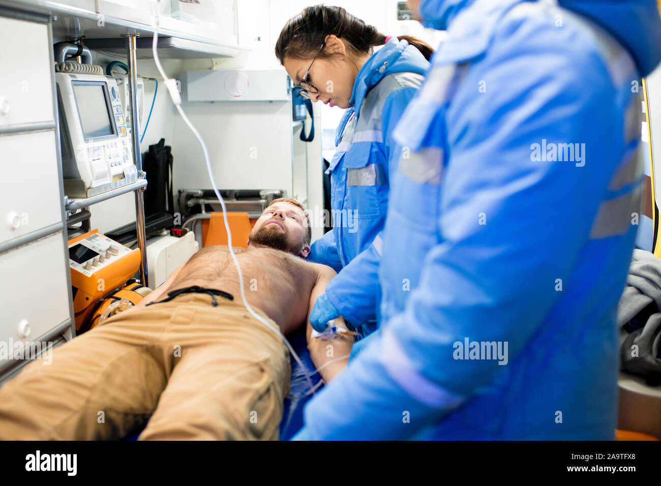 One of two paramedics in uniform giving first aid to sick shirtless man ...