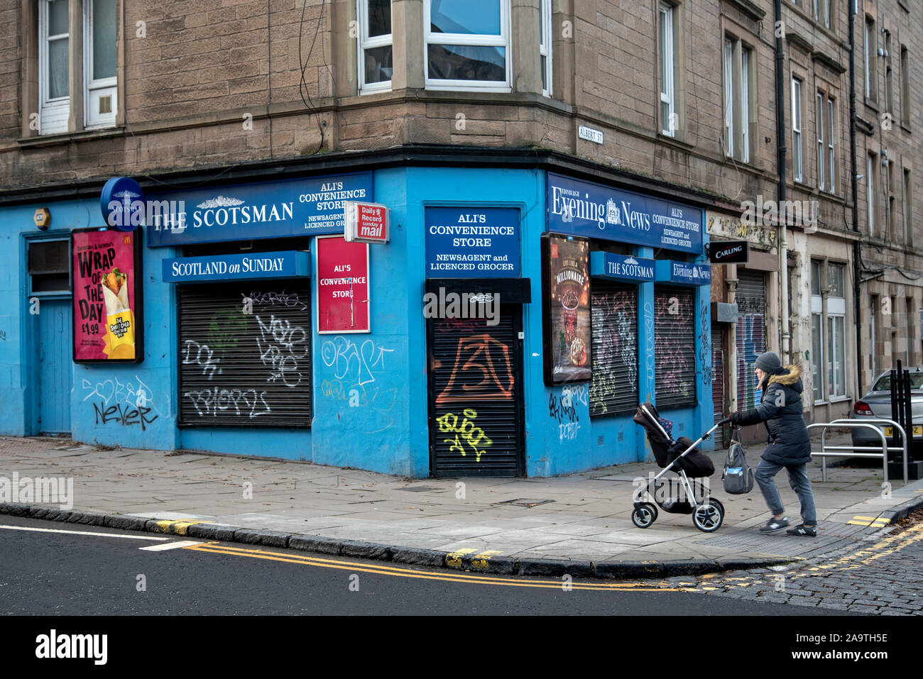 Woman pushing a buggy past a closed corner shop on Easter Road ...