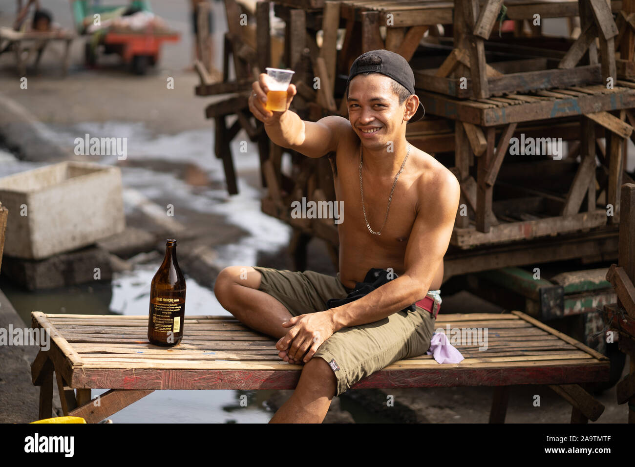 A young smiling Filipino man offers a glass of beer to the photographer ...