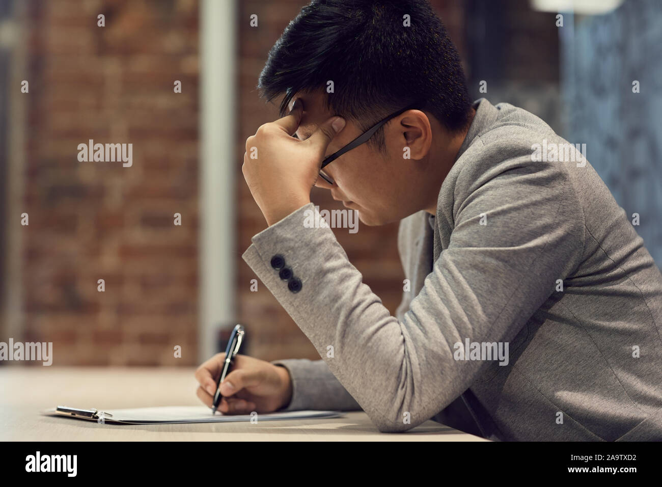 Side view portrait of young Asian man writing on clipboard while ...