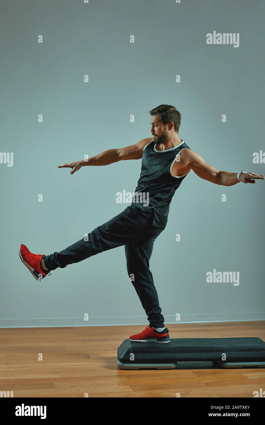 muscular young man training on step platforms on the gray background in ...