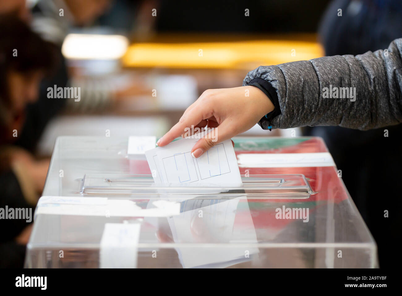 A woman casts her envelope vote into a transparent plastic ballot box ...