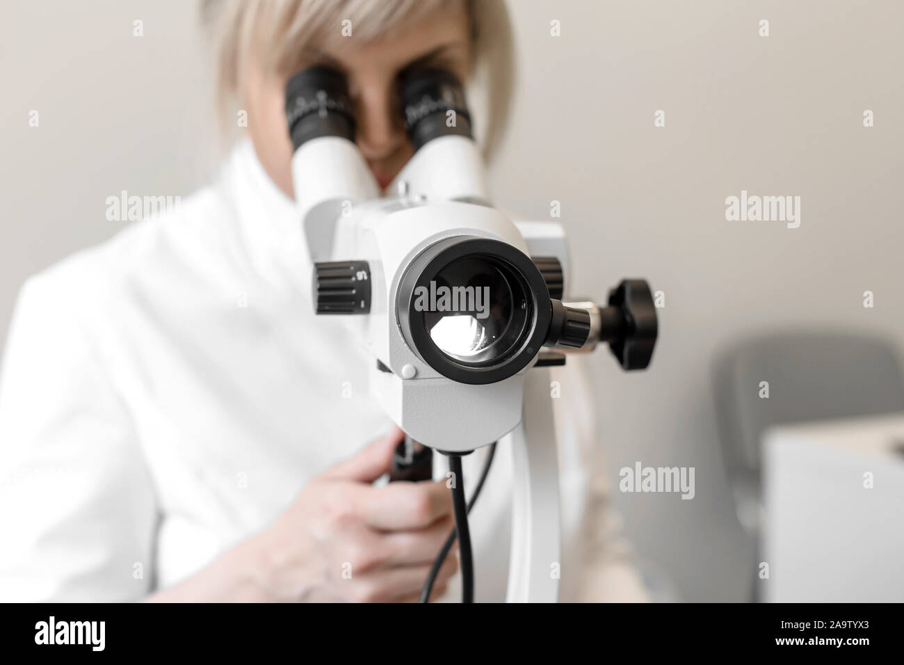 Female blond doctor gynecologist looks through a colposcope ...