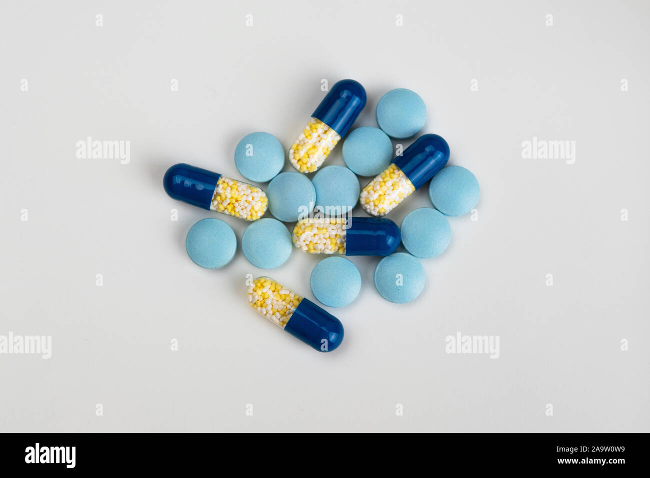 Blue and yellow pills and capsules on light grey background. Drug ...