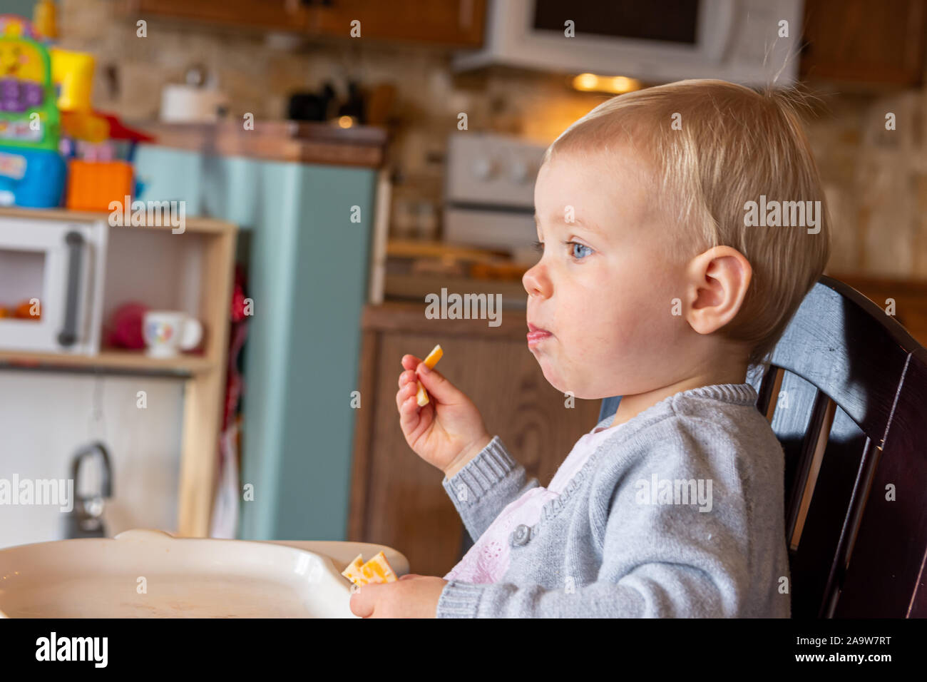 A very cute little girl sitting in her high chair having a snack Stock ...