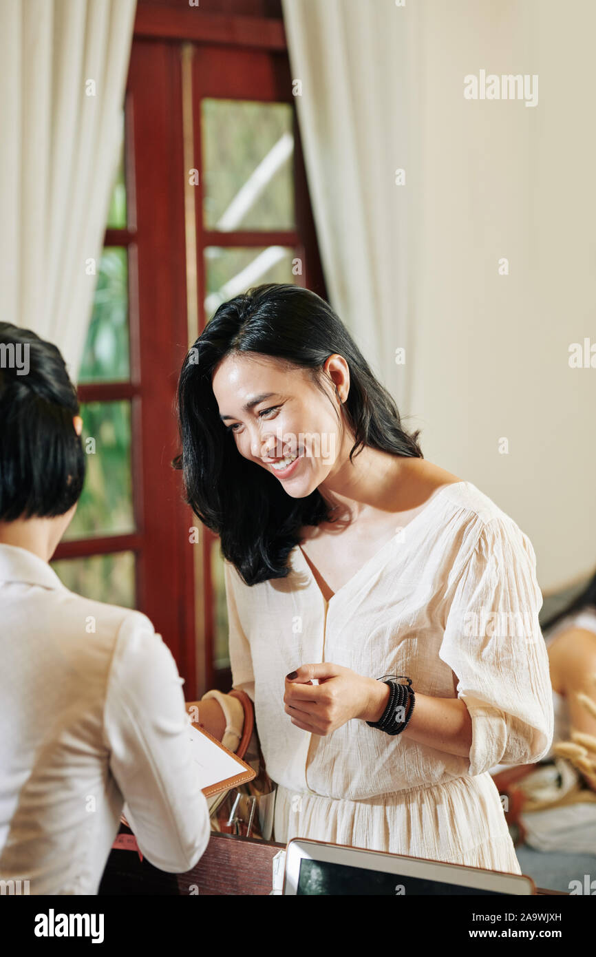 Happy young Asian woman taking questionnaire from hands of receptionist ...