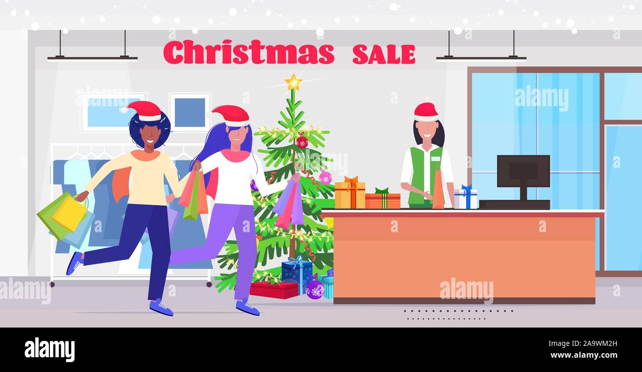 girls in santa hats with shopping bags standing at cash desk with ...