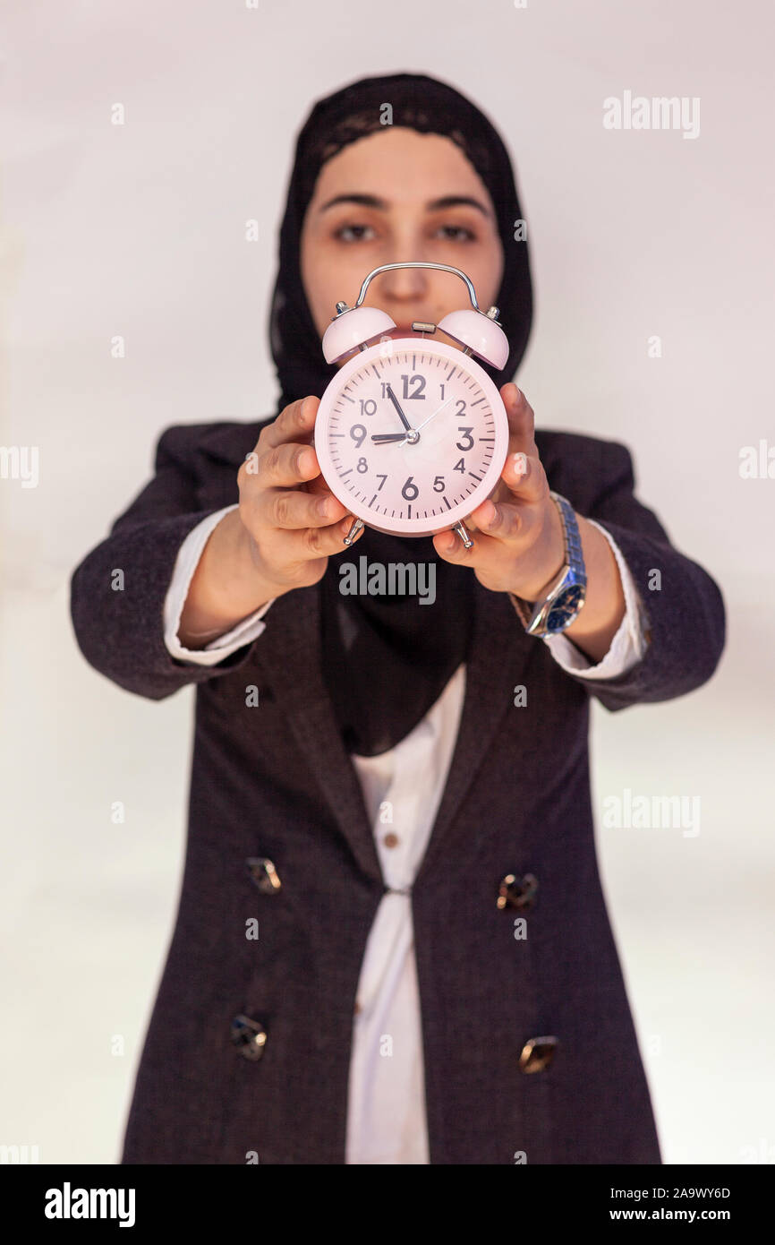 Young Muslim businesswoman in hijab holding pink vintage alarm clock ...