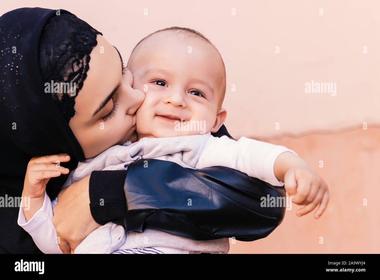 Young Muslim woman in hijab holding her 1-year-old baby boy, hugging ...
