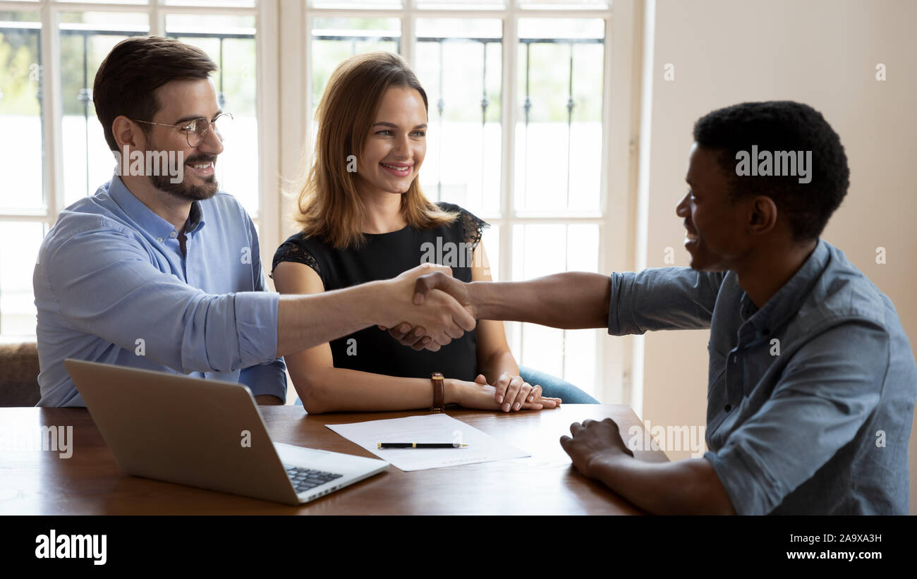 Young smiling clients shaking hands with african american financial ...