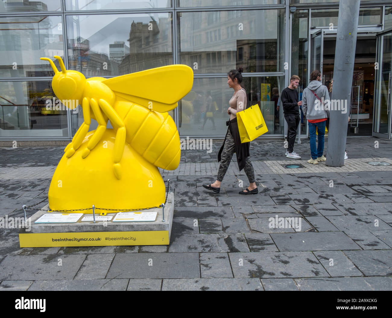 Lady in a yellow coat walking past a Manchester Bee painted yellow ...