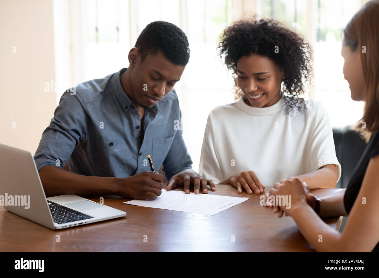 Happy young banking worker watching african ethnicity client signing ...