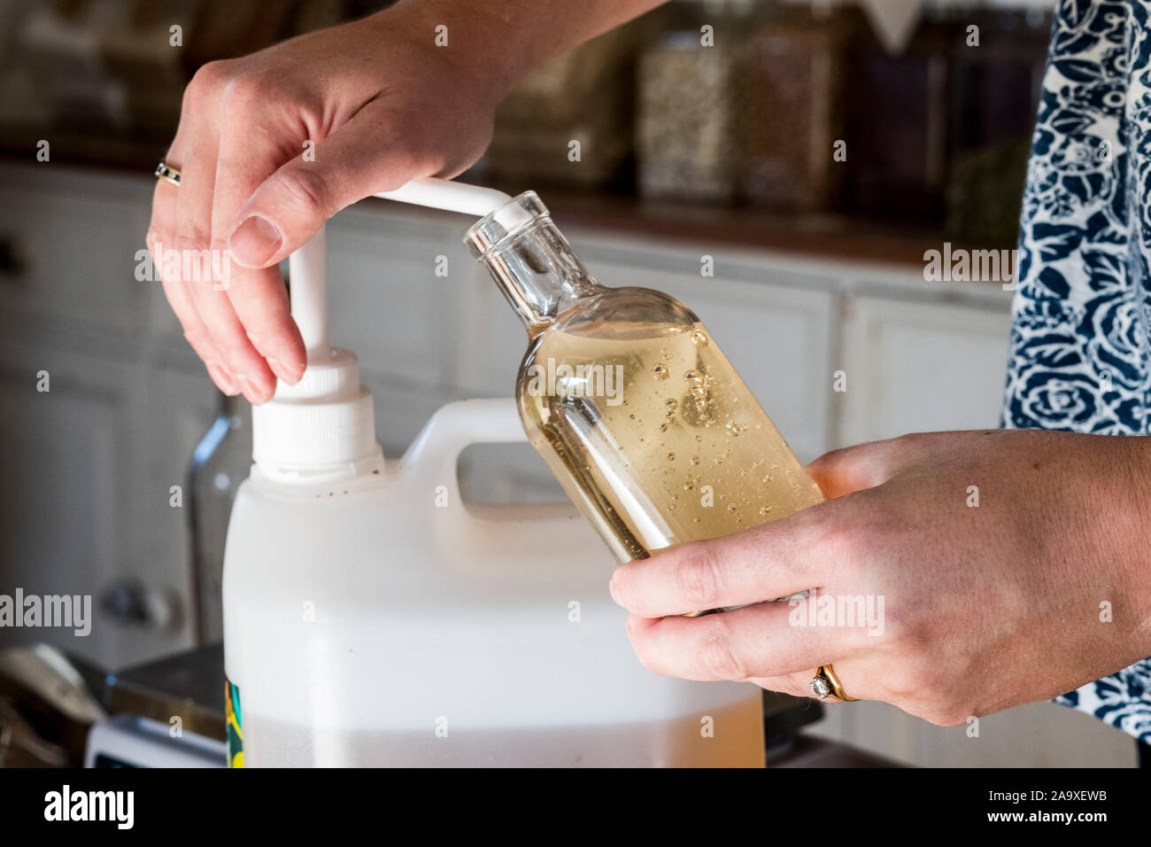 Close up of person standing in a kitchen, decanting liquid from plastic ...