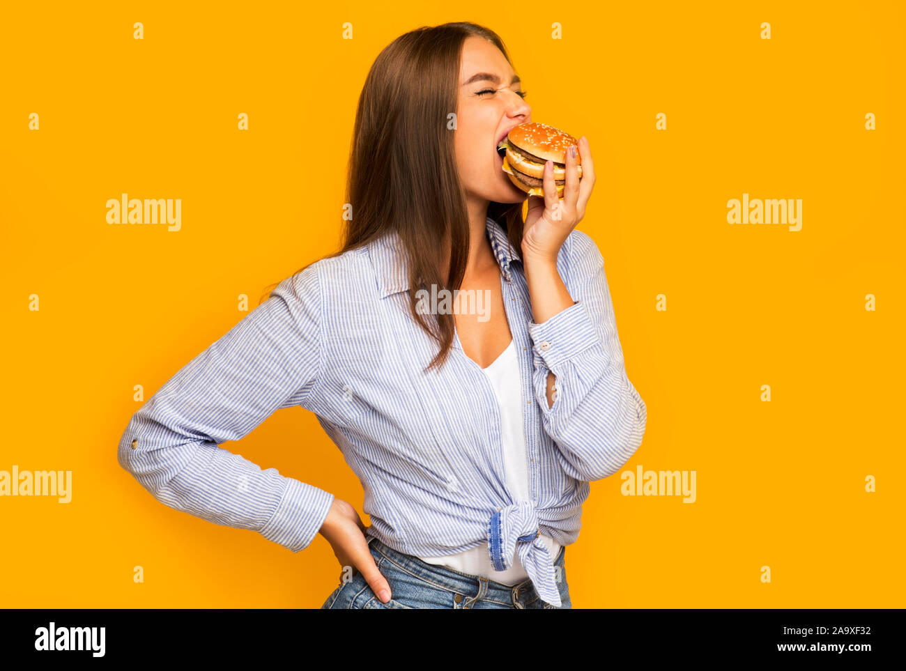 Hungry Girl Eating Burger Standing Over Yellow Background, Studio Shot ...