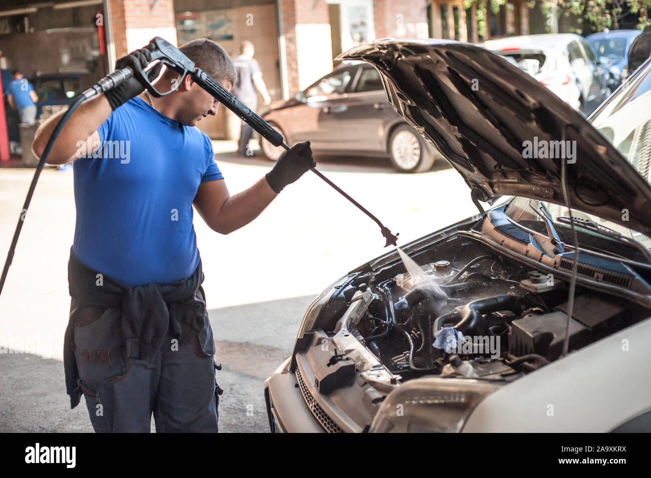 Car mechanic washes the car engine with pressurized water at service ...
