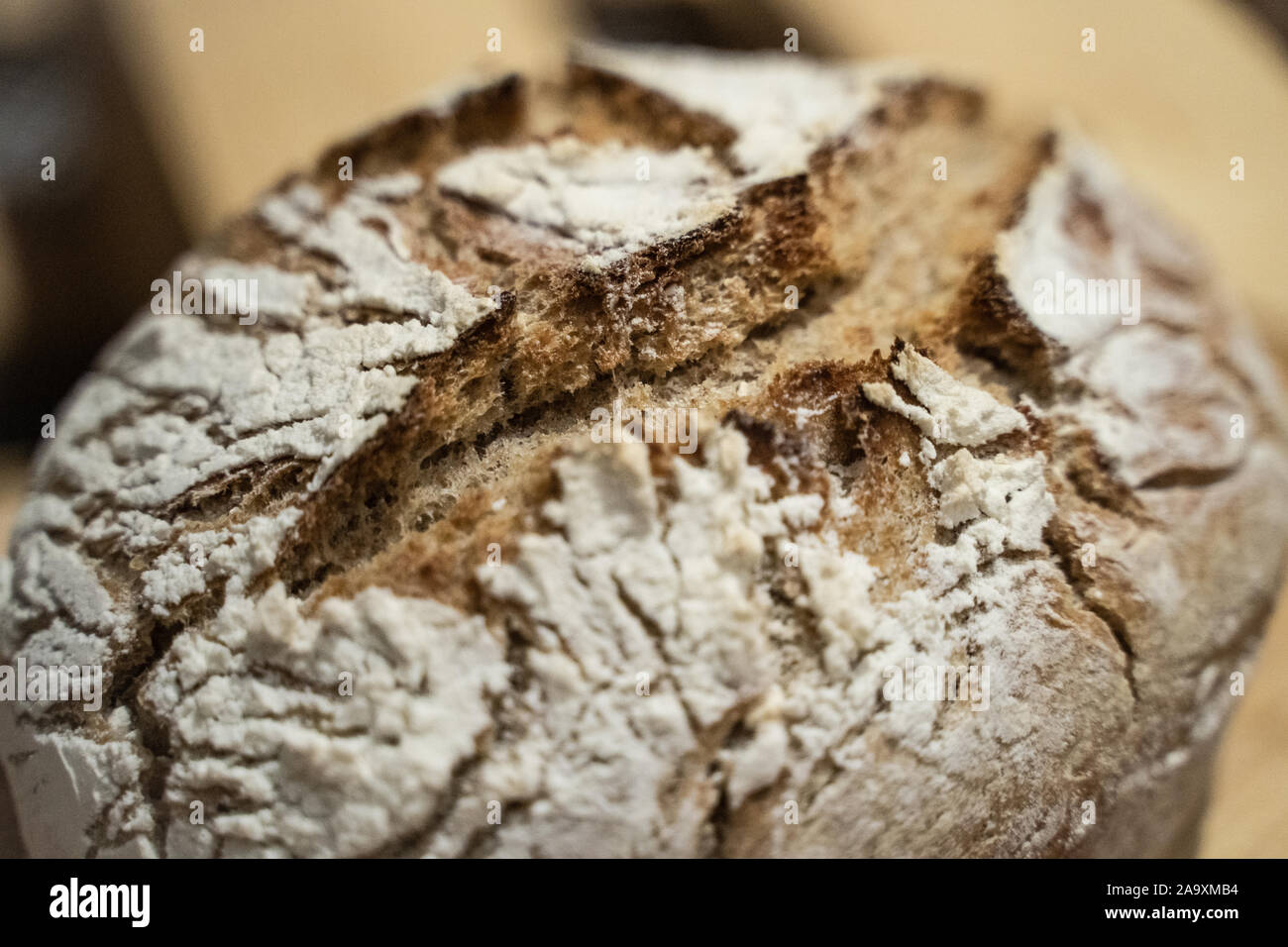 A fresh crusty rustic loaf of sourdough bread sat on a wooden bread ...