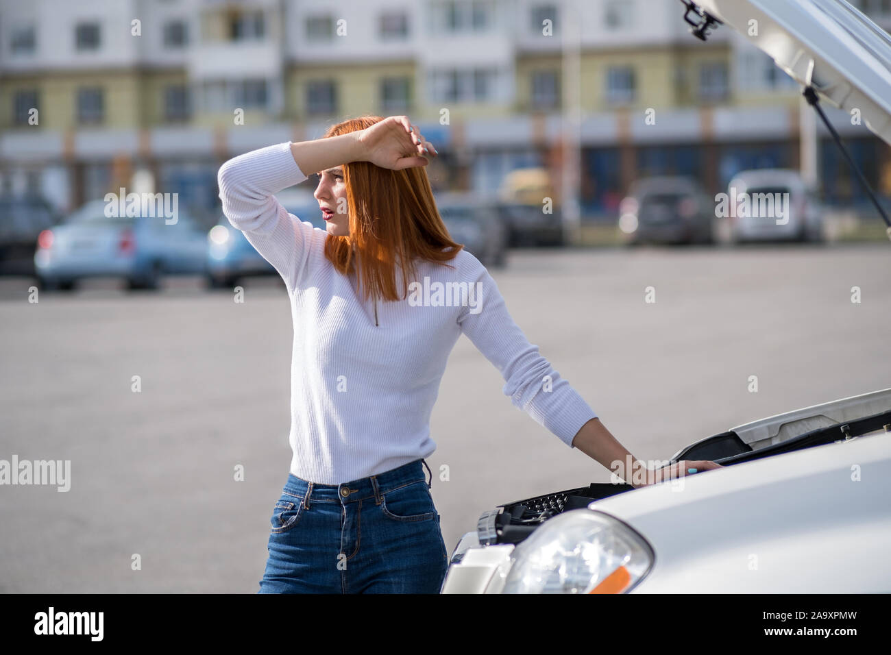 Young stressed woman driver standing near broken car with open hood ...