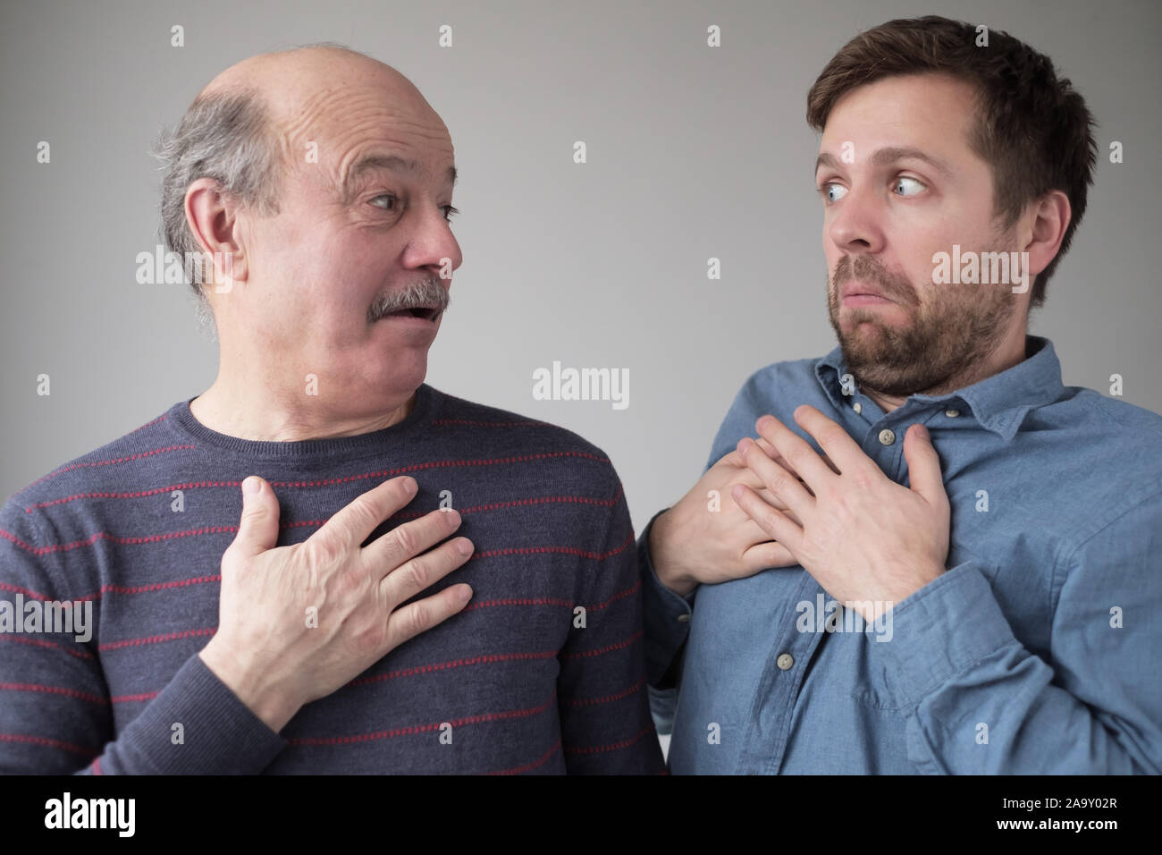 Confused mature father and son looking on each other with astonishment ...