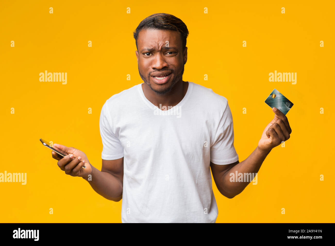 Confused Guy Holding Smartphone And Credit Card Posing In Studio Stock ...