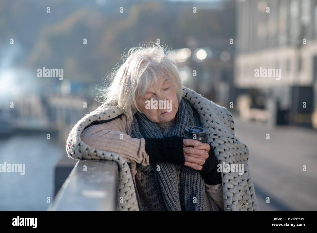 Grey-haired homeless woman standing on the bridge and drinking tea ...