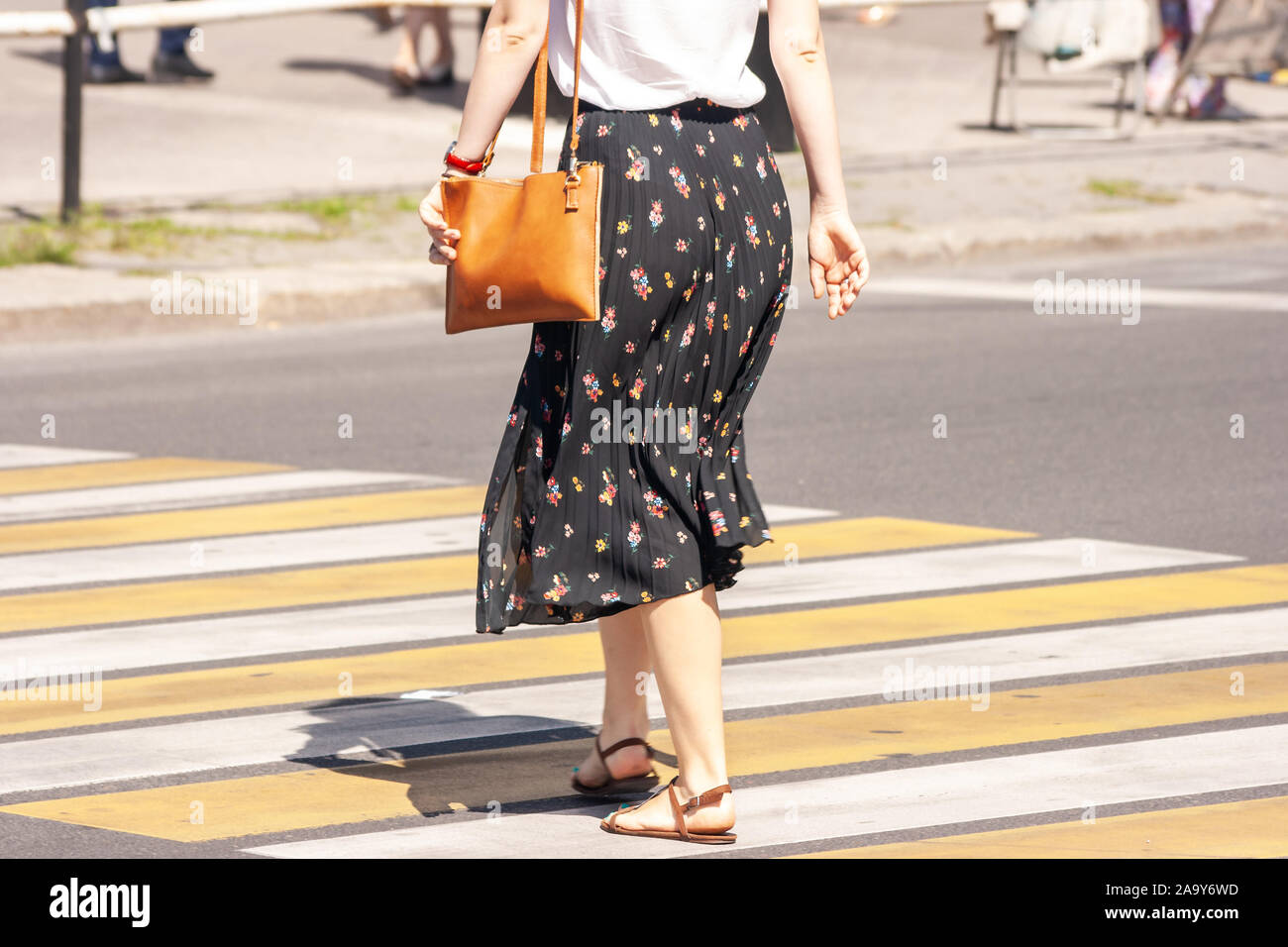 woman crossing the road at a crosswalk in the city on summer day. legs ...