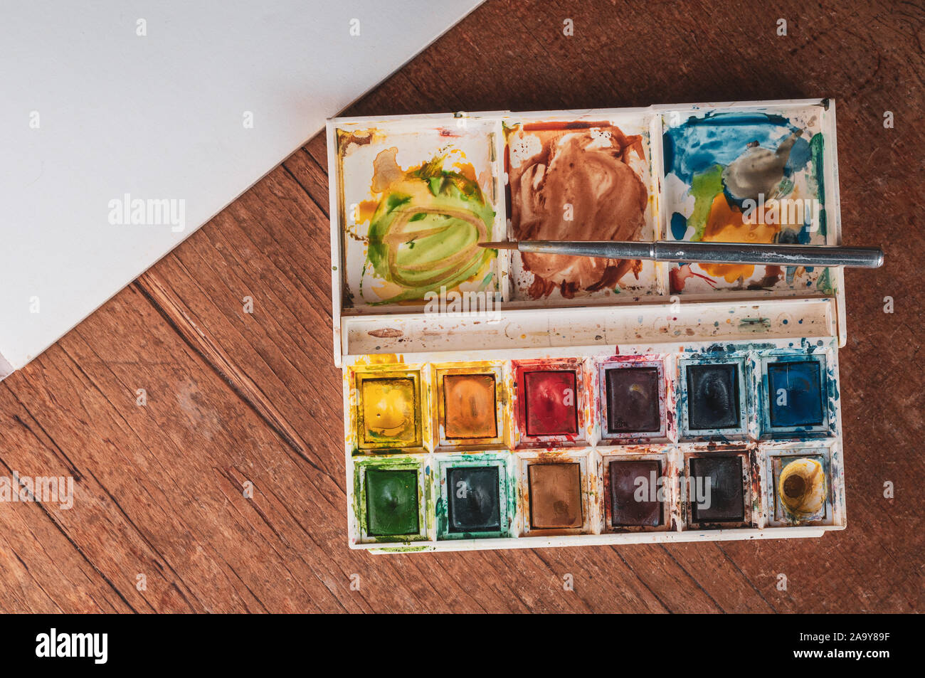 messy box of watercolour paints and brush on wooden table with white ...