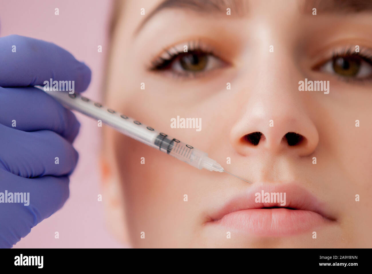 Doctor in gloves giving woman botox injections in lips, on pink ...