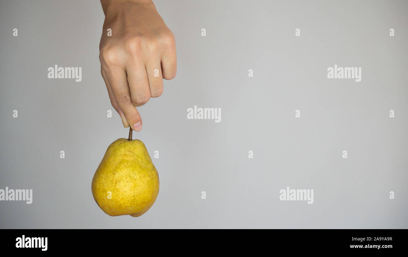 Yellow pear dangling by stem in woman's hand. Negative space. Copy ...