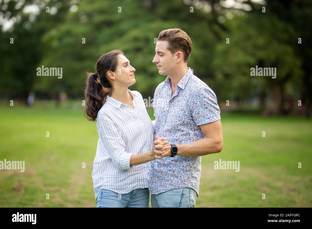 Outdoor shot of young couple in love joyful in the park through grass ...
