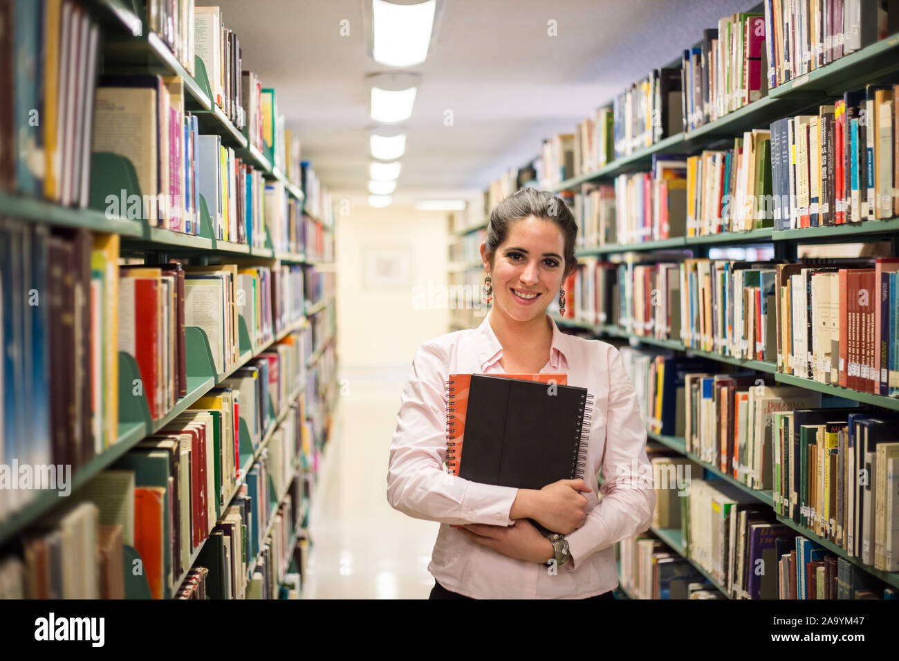 In the library - pretty female student with books working in a high ...