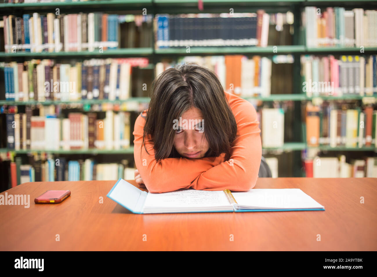 In the library - lazy bored pretty female student with books working in ...