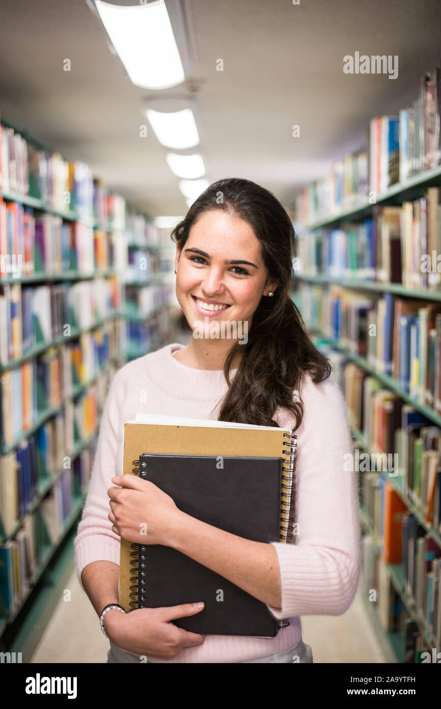 In the library - pretty female student with books working in a high ...