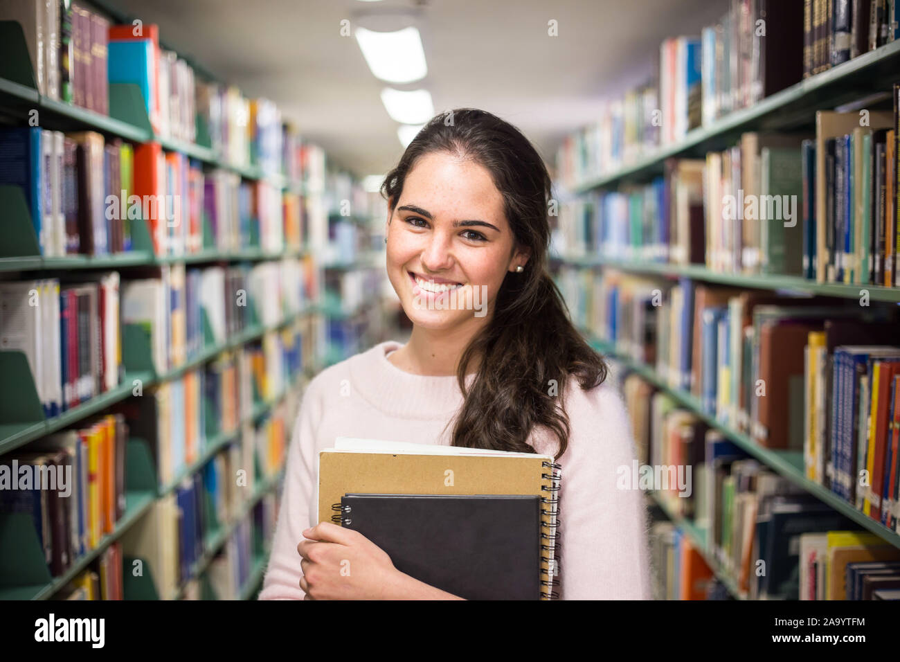 In the library - pretty female student with books working in a high ...