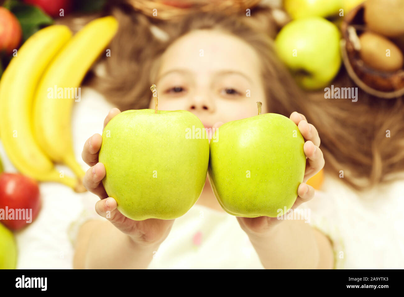 child or cute baby girl laying with colorful fruits hold green apple ...