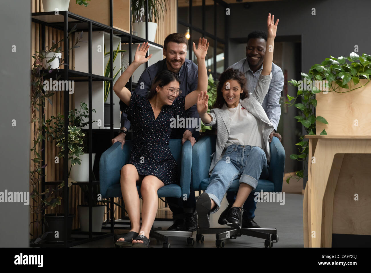 Overjoyed young diverse colleagues having fun, riding on chairs Stock ...