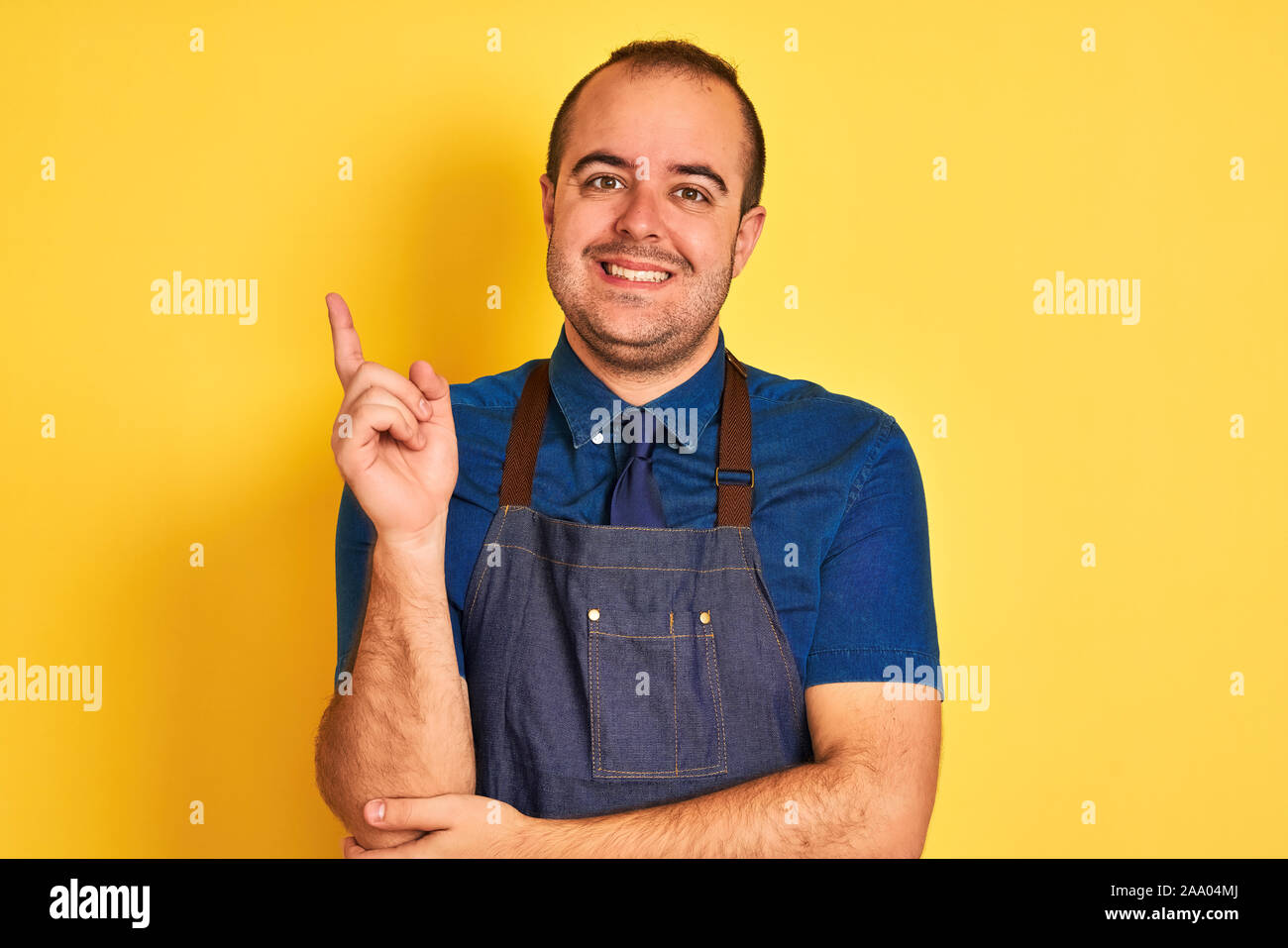 Young shopkeeper man wearing apron standing over isolated yellow ...