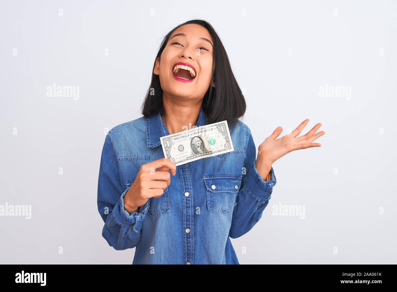 Young beautiful chinese woman holding one dollar standing over isolated ...