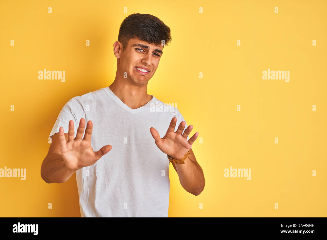 Young indian man wearing white t-shirt standing over isolated yellow ...
